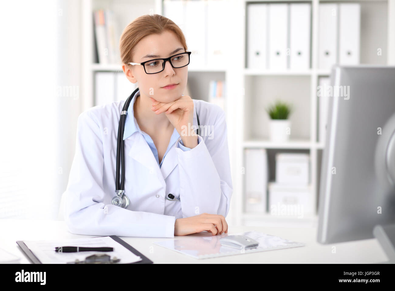 Young brunette female doctor sitting at the table and working by ...
