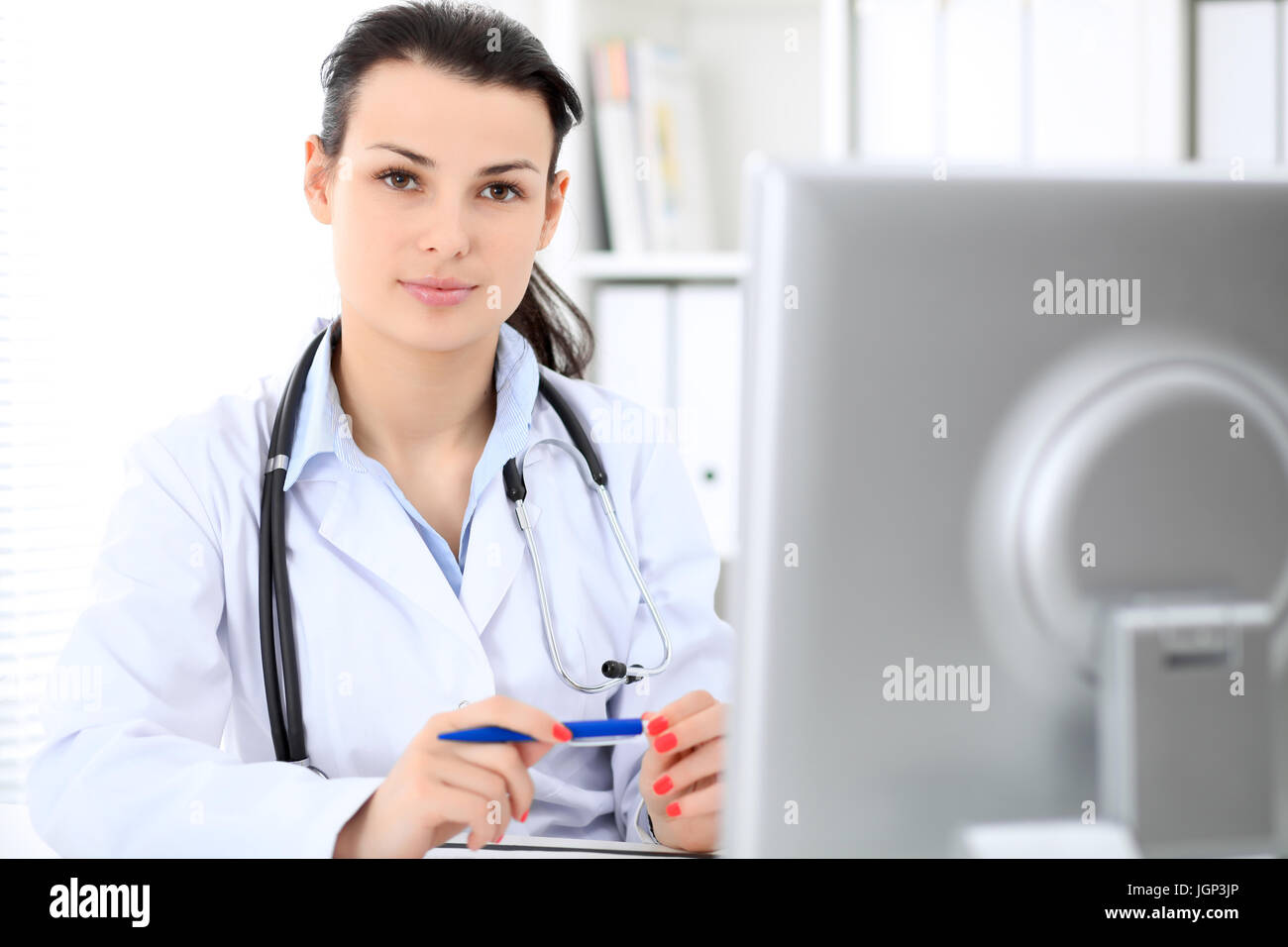 Young brunette female doctor sitting at the table and working by ...