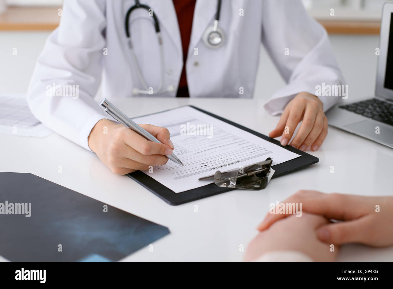 Close up of a female doctor filling up an application form while ...