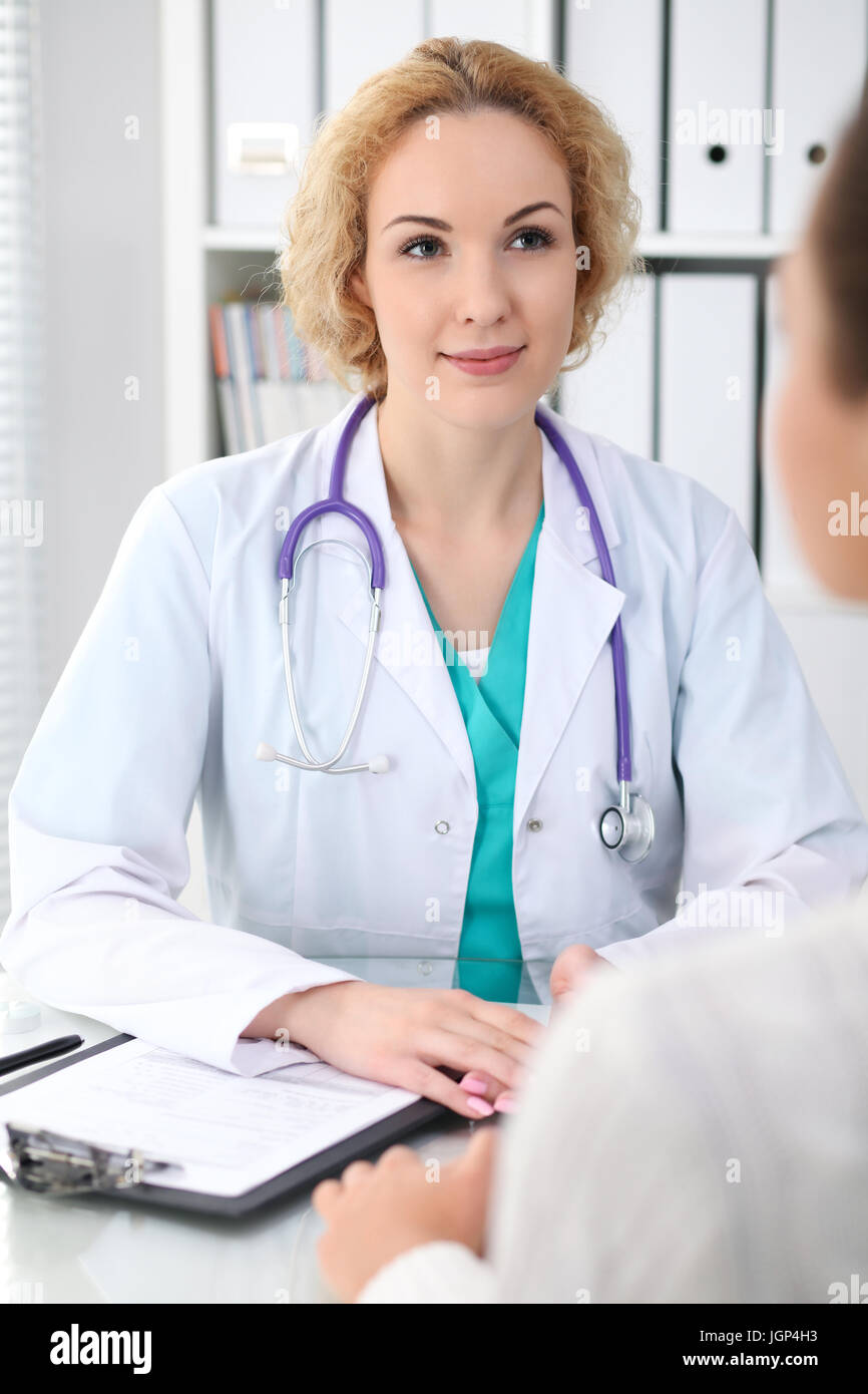 Happy blonde female doctor sitting at the table and filling up medical ...