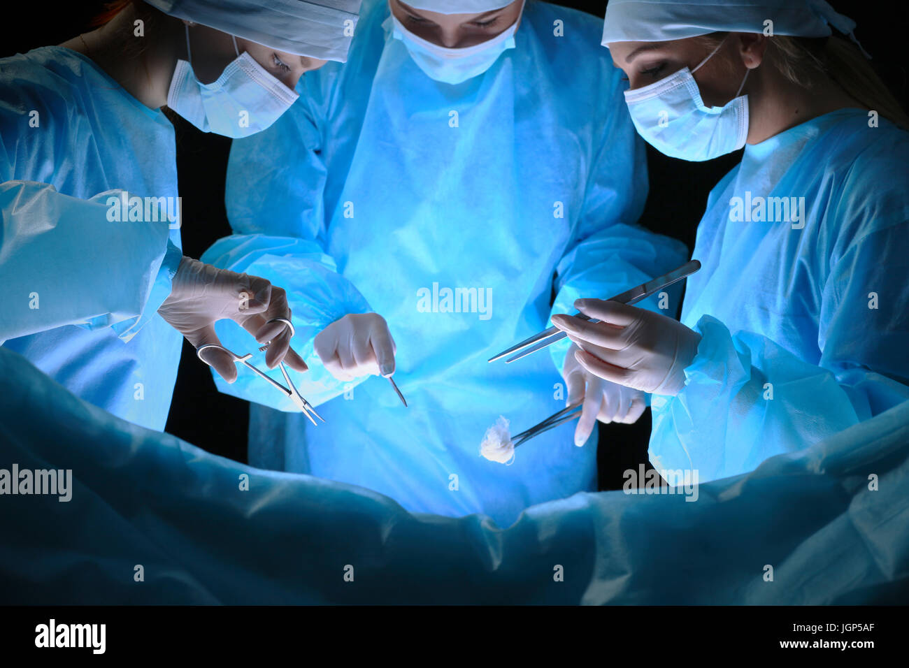 Group of surgeons at work in operating theater toned in blue. Medical ...