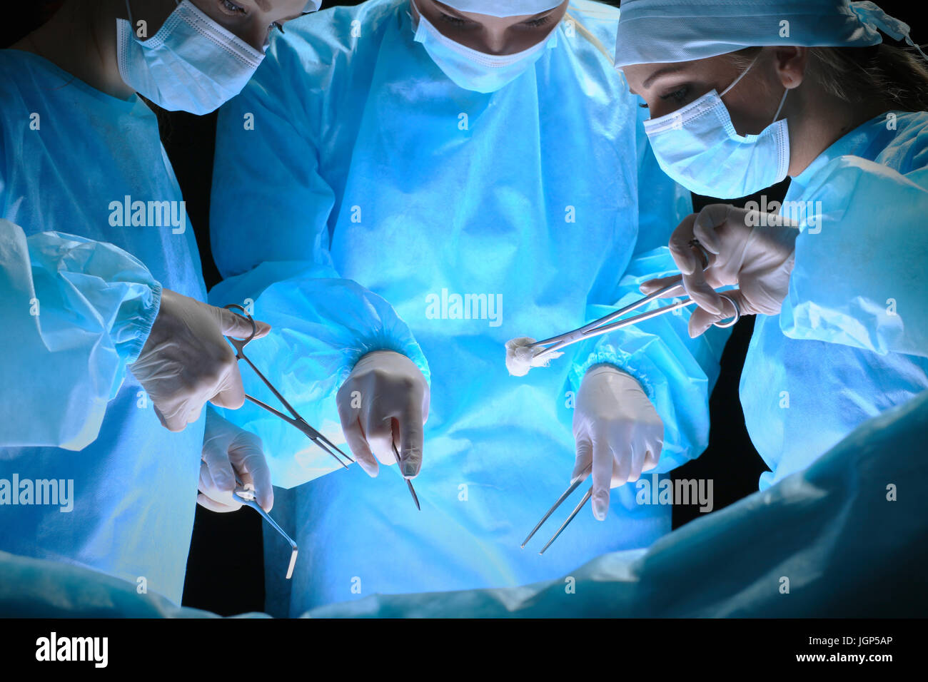 Group of surgeons at work in operating theater toned in blue. Medical ...