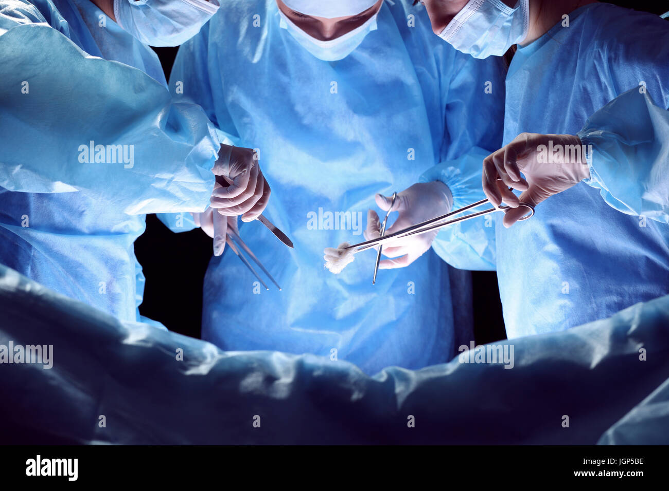 Group of surgeons at work in operating theater toned in blue. Medical ...