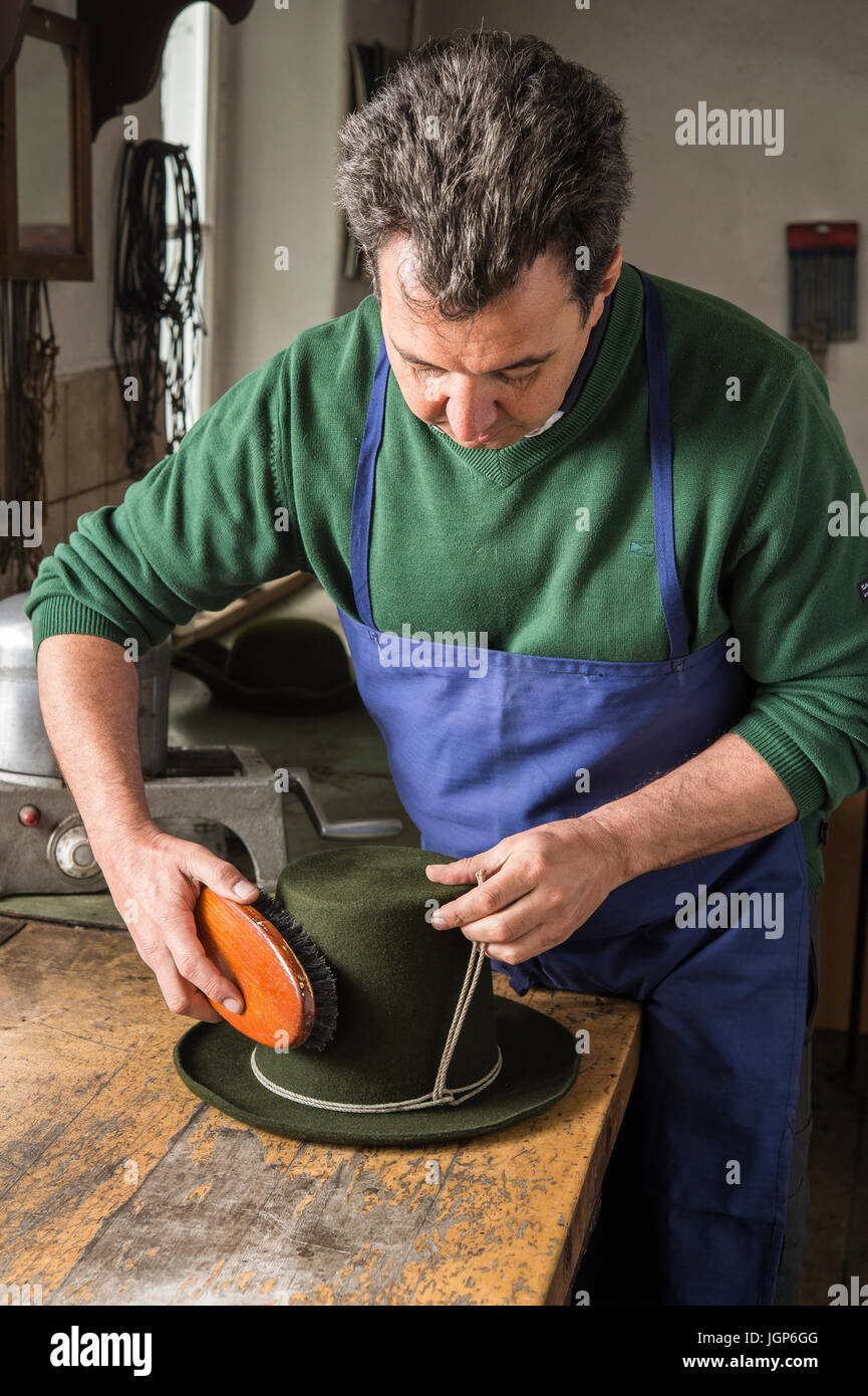 Man brushing a dry wool felt hat, holding shaping cord in his hand ...