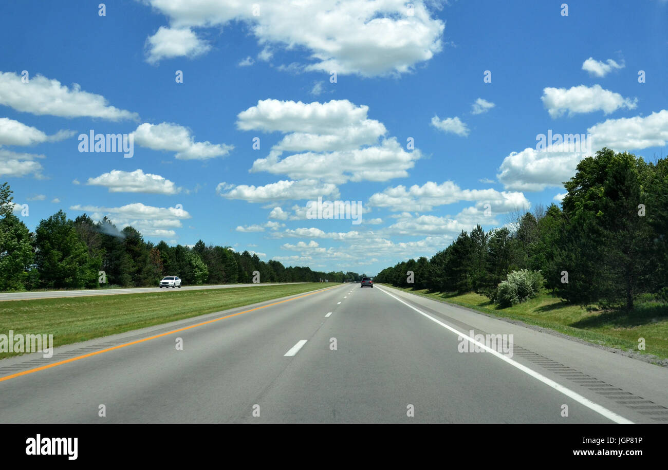 Highway with cars in distance, sunny skies with a few puffy clouds ...