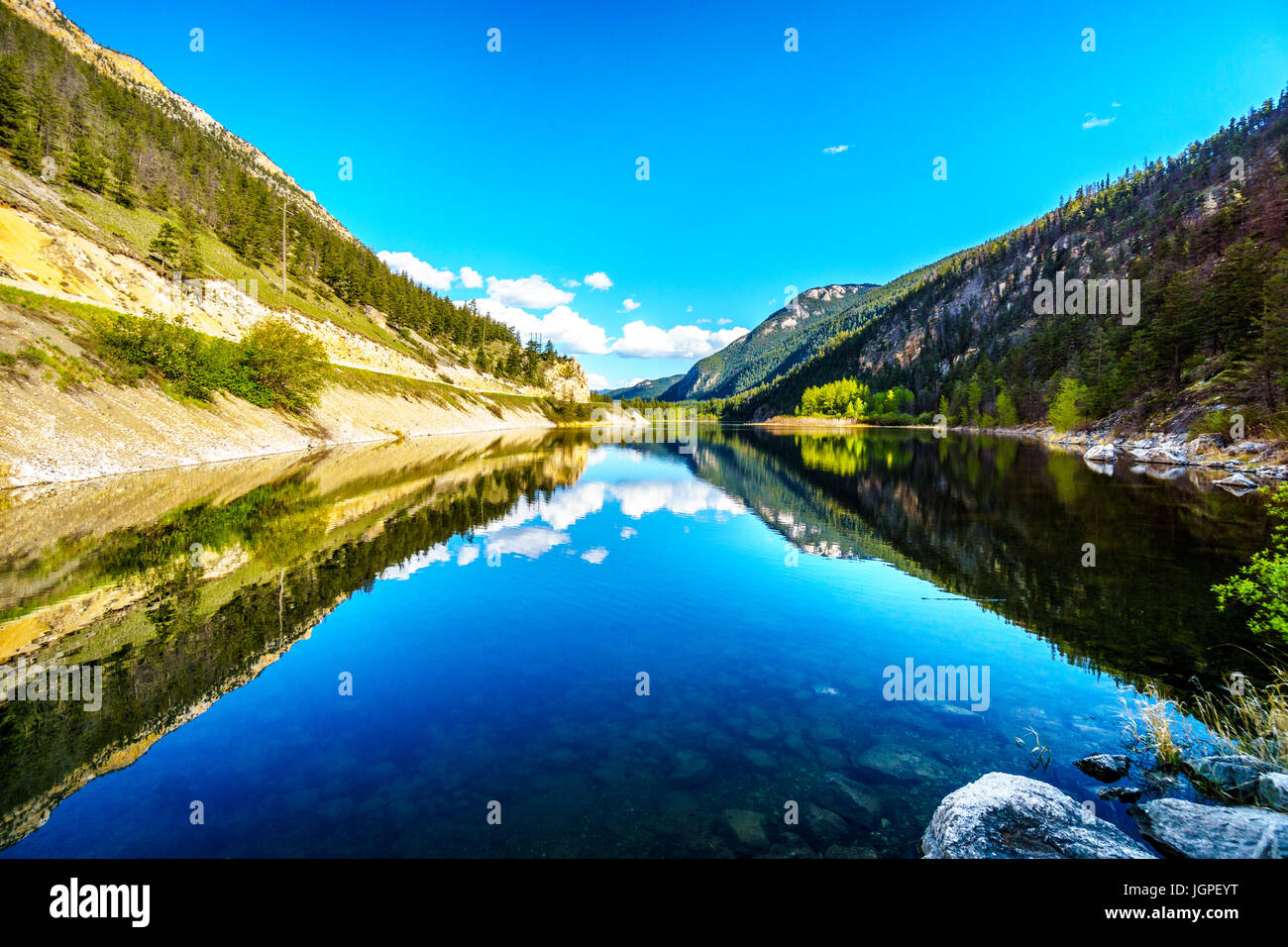 Blue sky, trees and mountains reflecting in the smooth surface on the ...