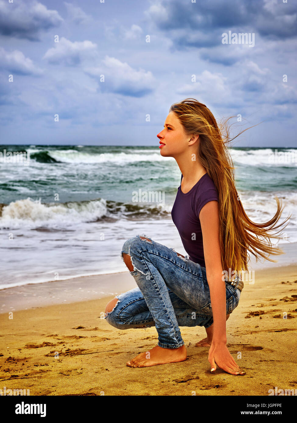 Girl on in sand beach looks thoughtfully into distance to last ray of ...