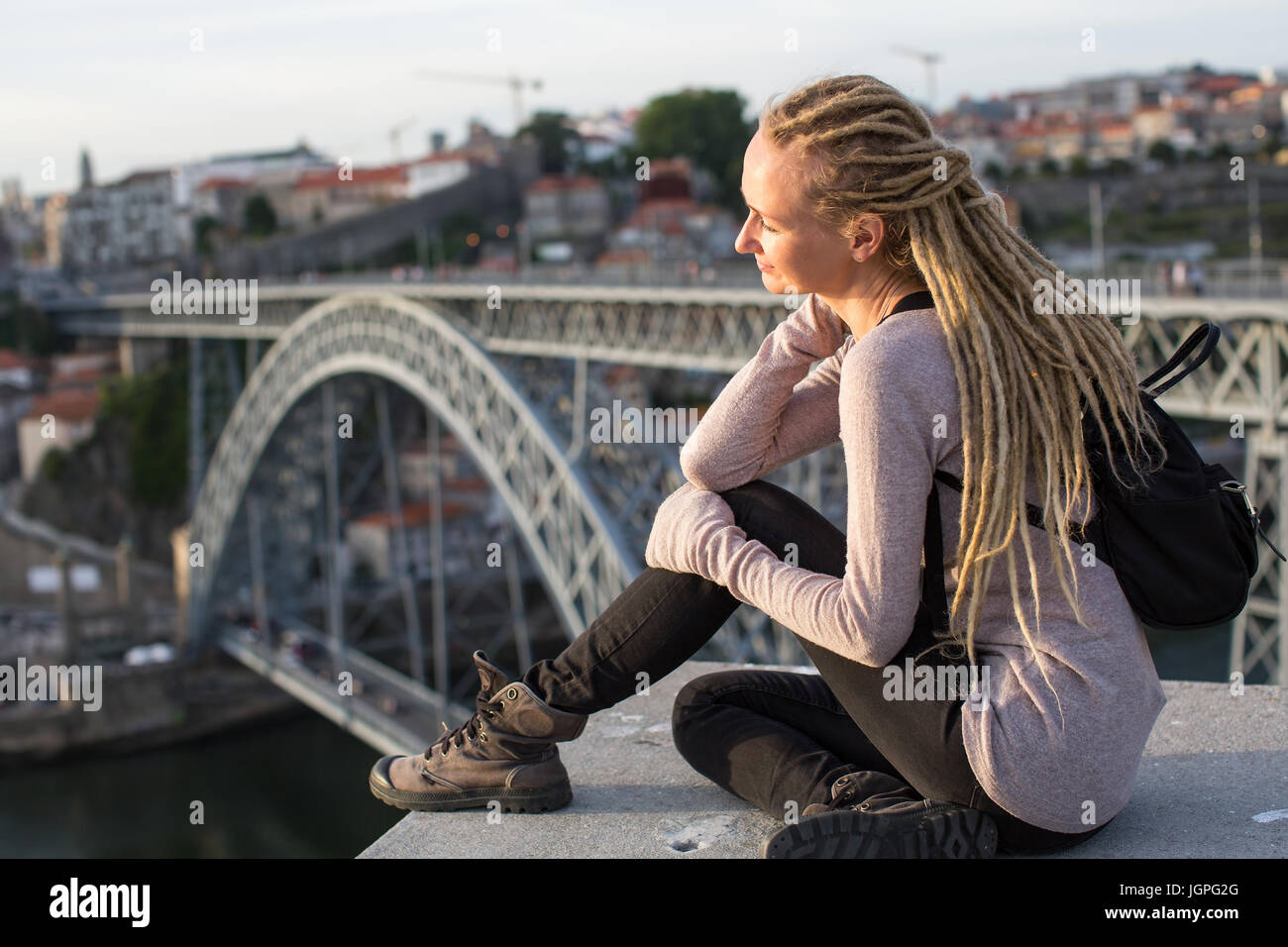 Young woman with blond dreadlocks sitting on the viewing platform ...