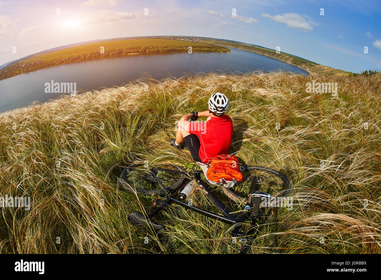 The attractive cyclist sitting on the grass on the meadow with mountain ...