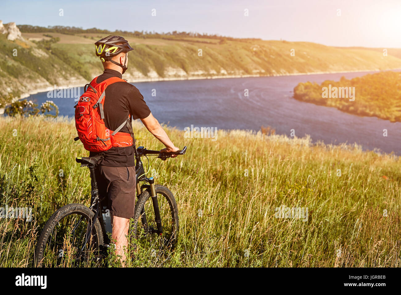 Rear view of the young cyclist stands with mountain bike on the green ...