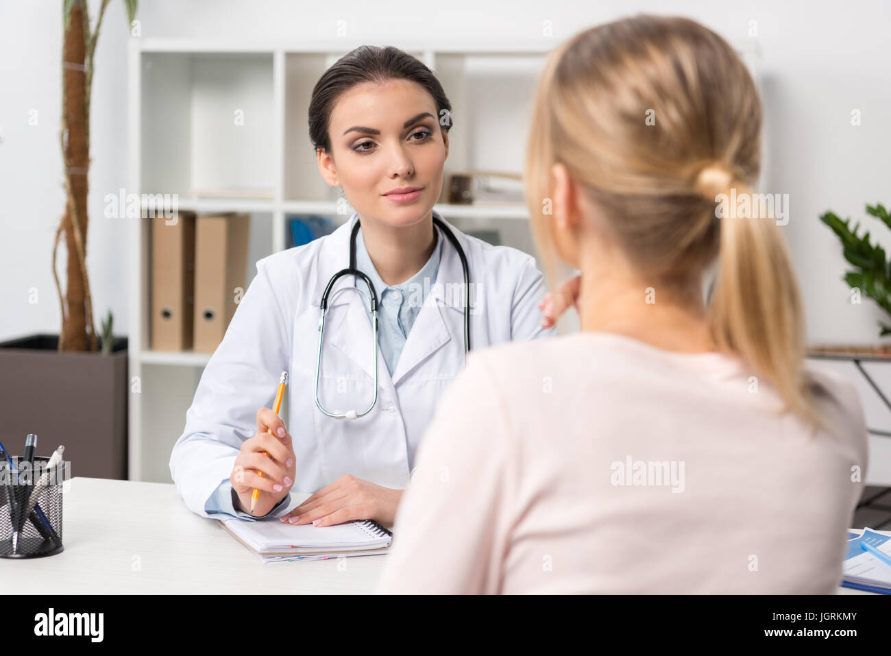 Young doctor with stethoscope taking notes while talking with patient ...