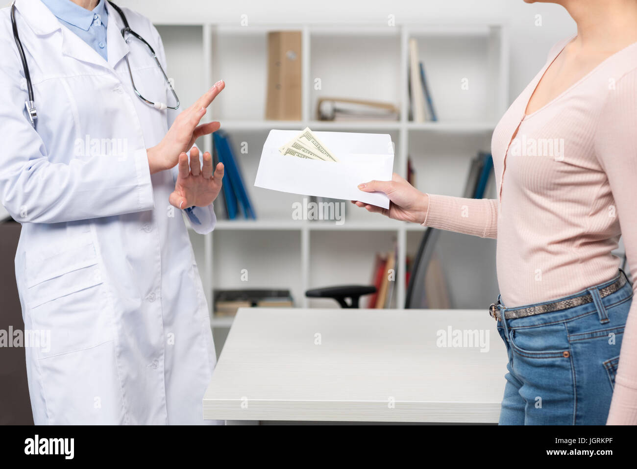 Cropped shot of patient giving envelope with dollar banknotes to doctor ...
