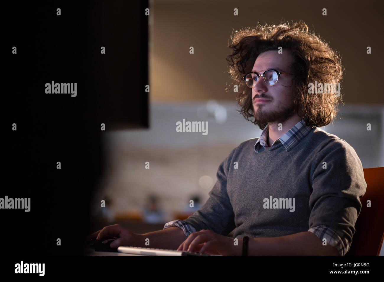 Young man working on computer at night in dark office. The designer ...