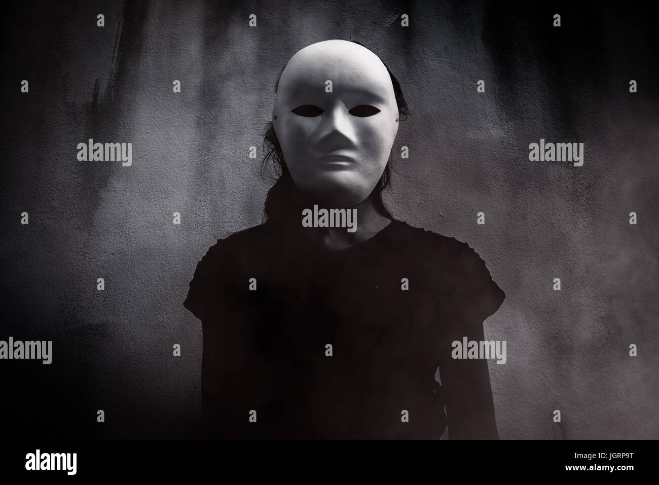 Mysterious woman in black wearing white mask hidden behind the dark ...