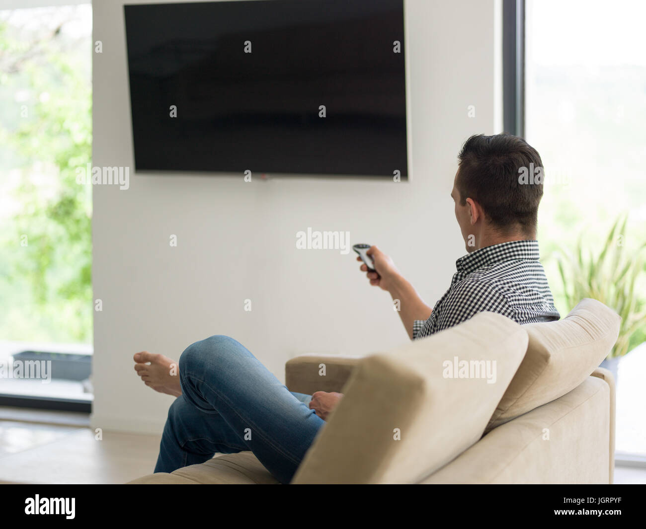 young handsome man enjoying free time watching television in his luxury ...