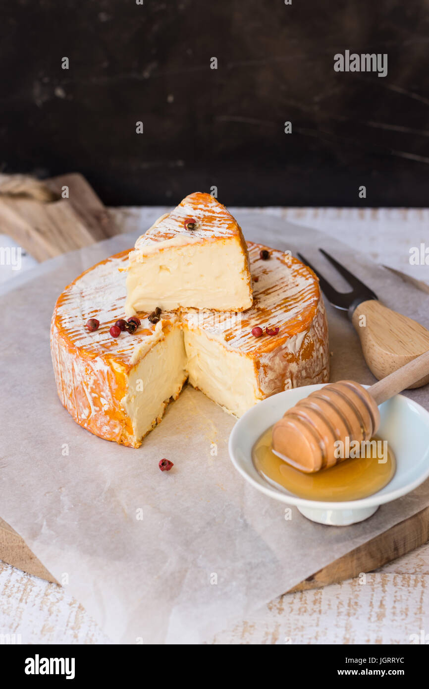 French soft cheese with orange rind on waxed paper, red pepper corns ...