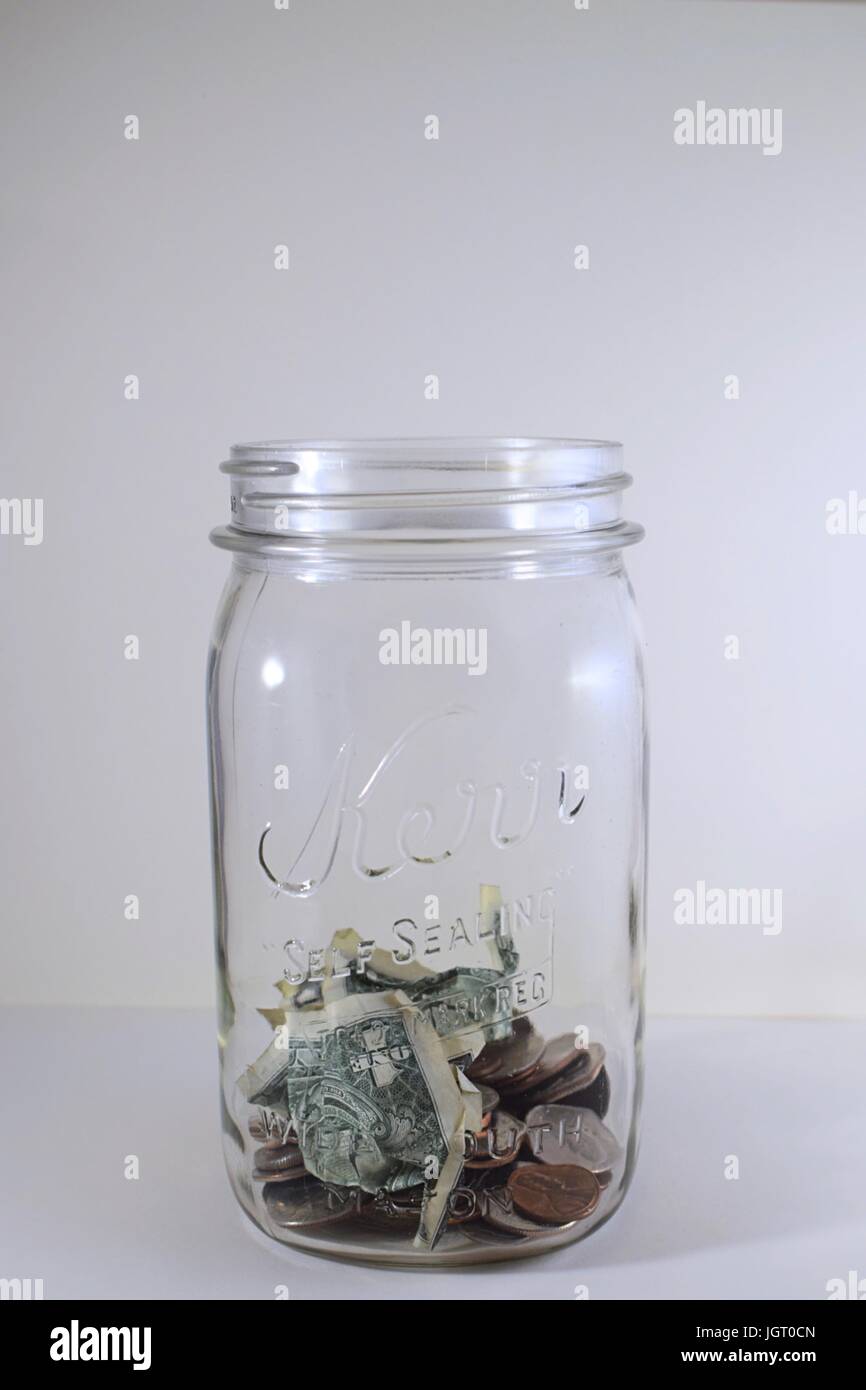 Kerr mason jar half filled with dollar bills and coins change on solid ...