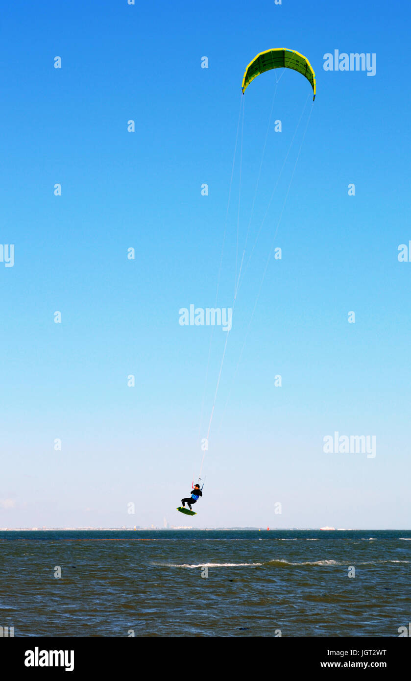 Kite surfer doing a jump at Lepe beach in the Solent against blue sky ...