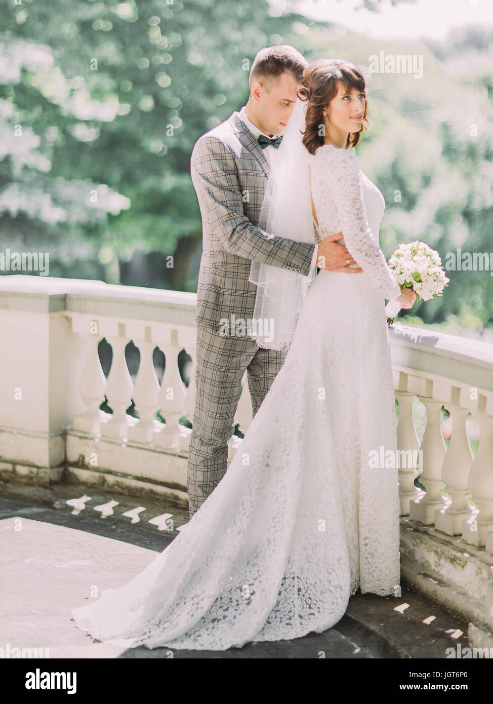 The full-length view of the groom hugging the bride back on the balcony ...