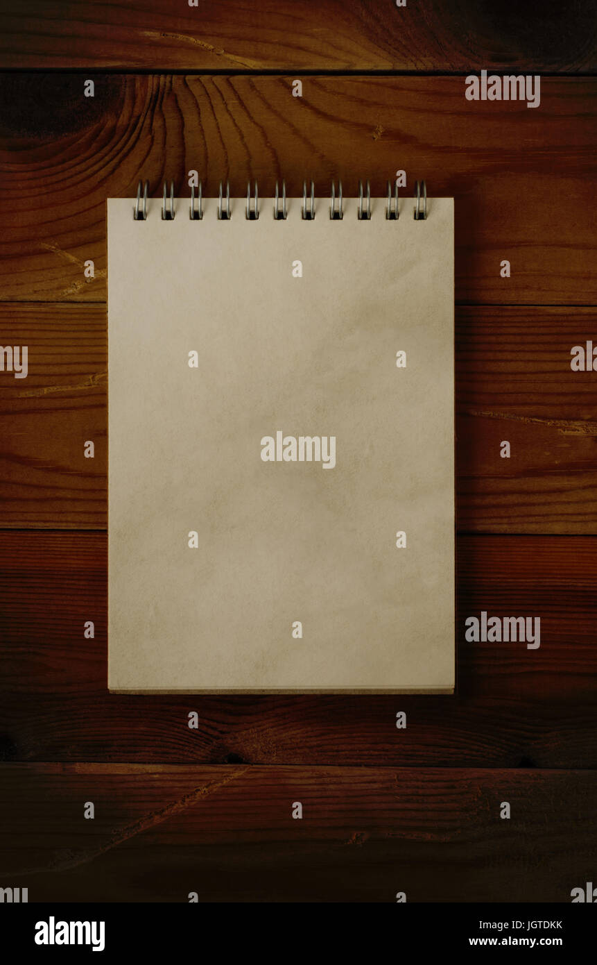 An opened, blank page of a spiral bound notebook on dark, weathered old ...