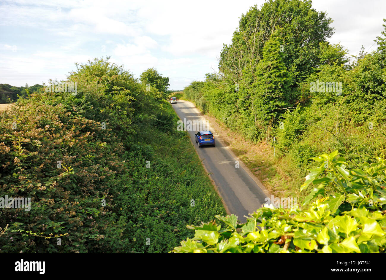 A narrow country road with two cars in the countryside at Felmingham ...