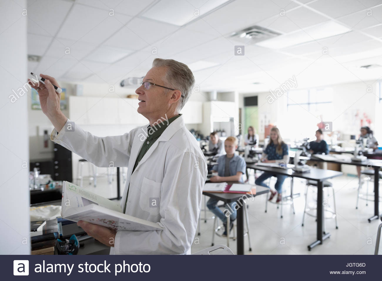 Students watching science teacher writing on whiteboard in laboratory ...