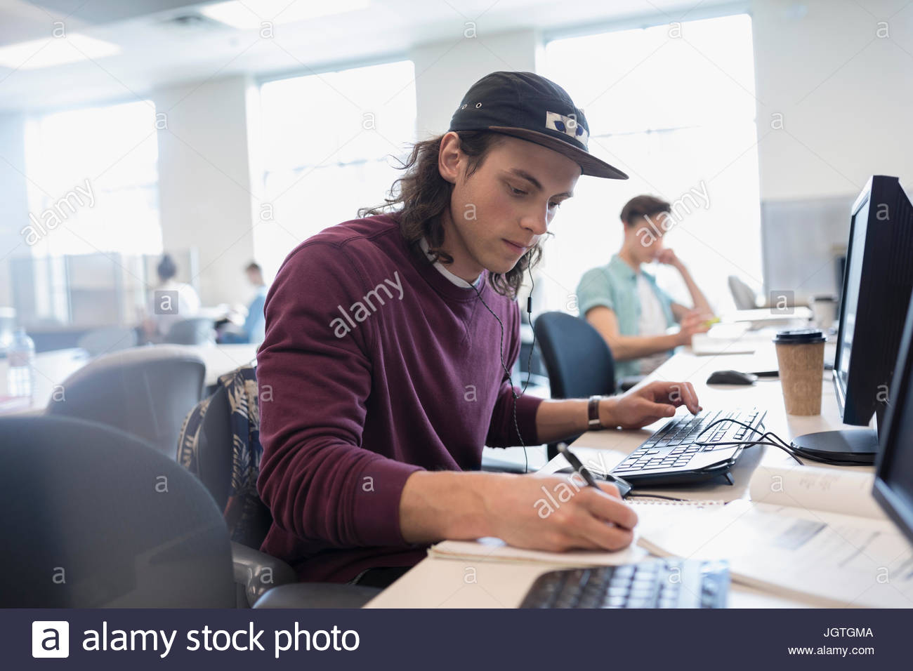 Male college student studying, researching at computer in library Stock ...