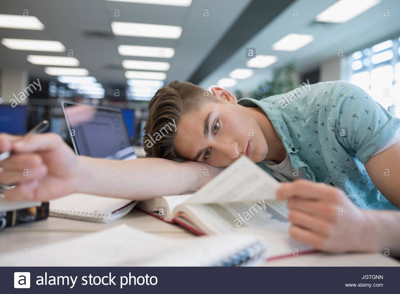 Tired male college student studying in library Stock Photo - Alamy