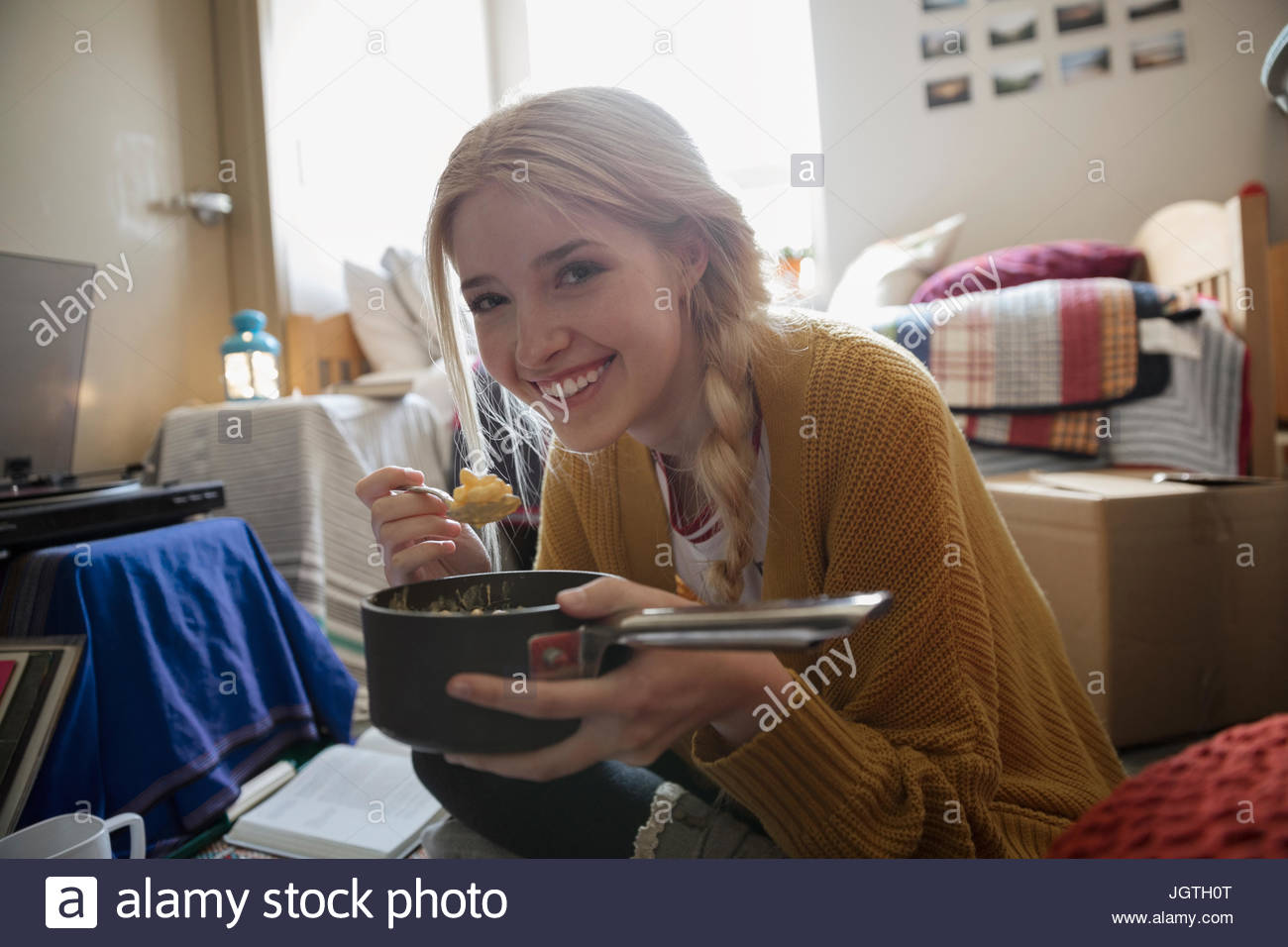 Portrait smiling female college student eating out of pot in dorm room ...
