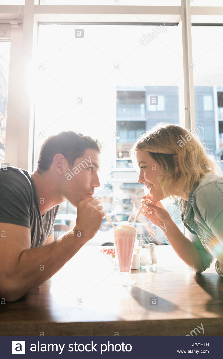 Young couple sharing milkshake at sunny diner table Stock Photo - Alamy