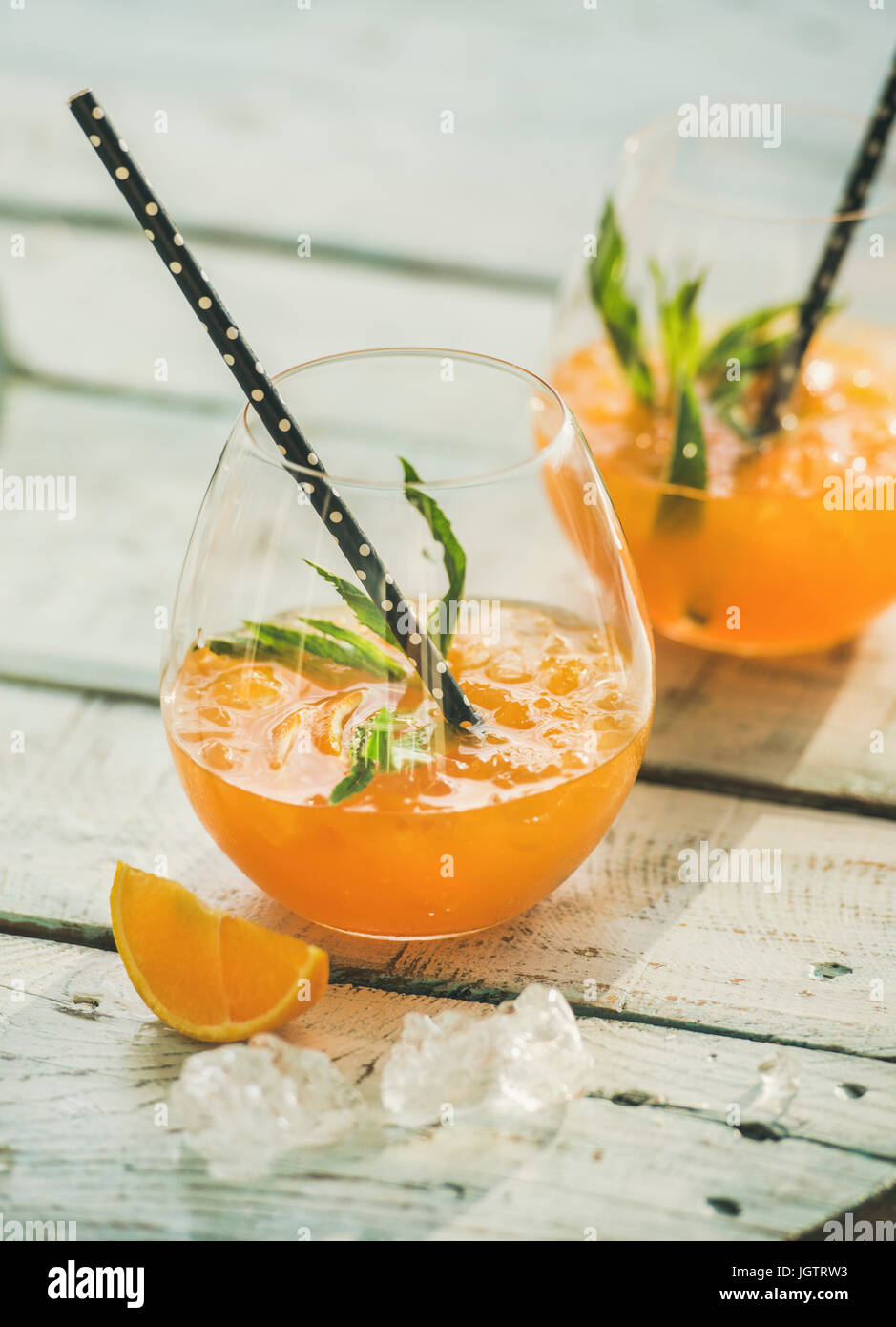 Refreshing cold alcoholic summer citrus cocktail with orange, peppermint and ice in stemless ...