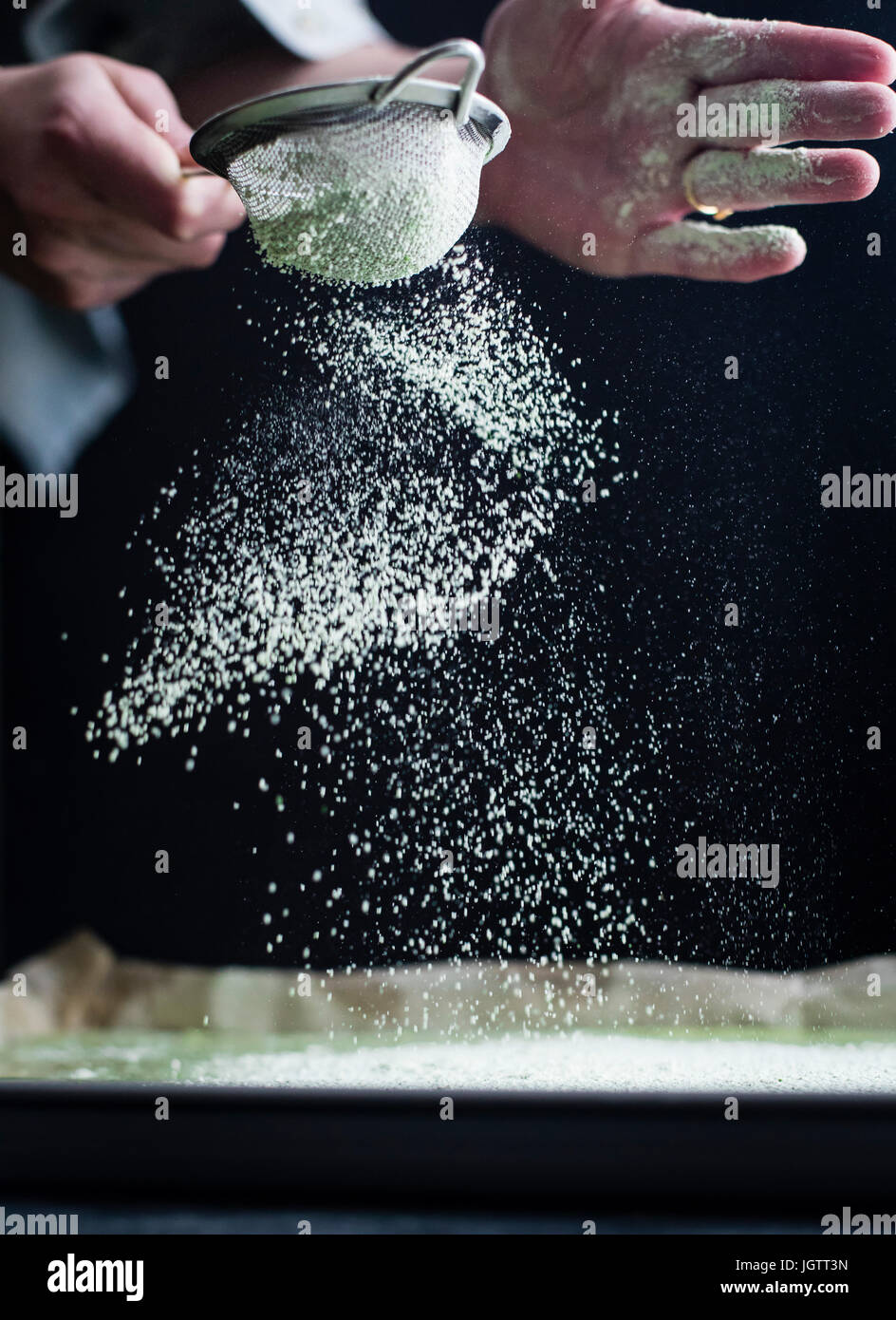A cooks hands sprinking icing sugar on to a baking tray Stock Photo - Alamy