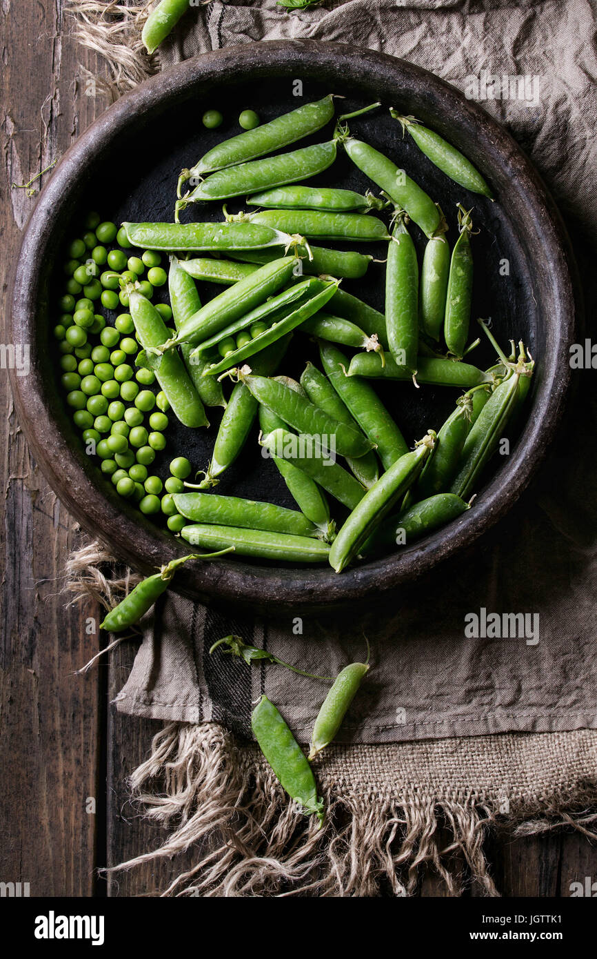 Young organic green pea pods and peas in terracotta tray over old dark ...