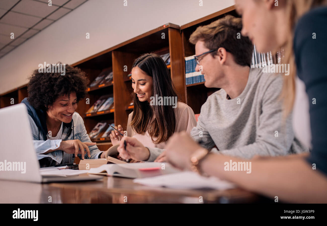 Young people sitting at table reading reference books for study notes ...