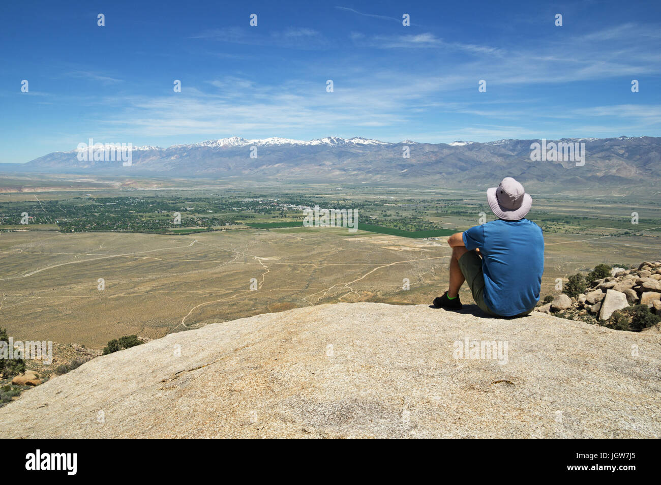 a man with a hat facing away sits on a rock overlook looking down at ...