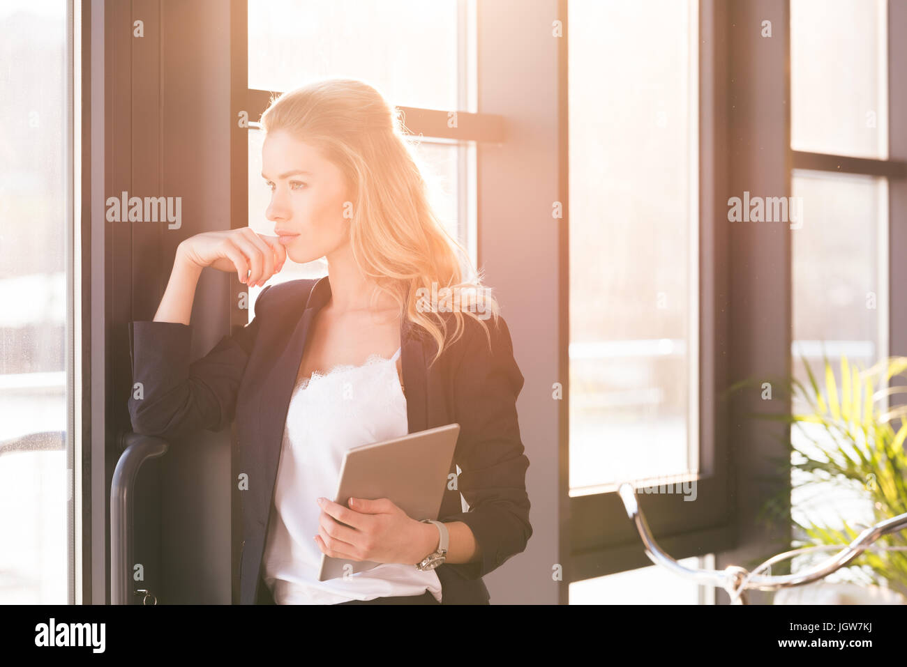 Beautiful young businesswoman holding digital tablet and looking away ...
