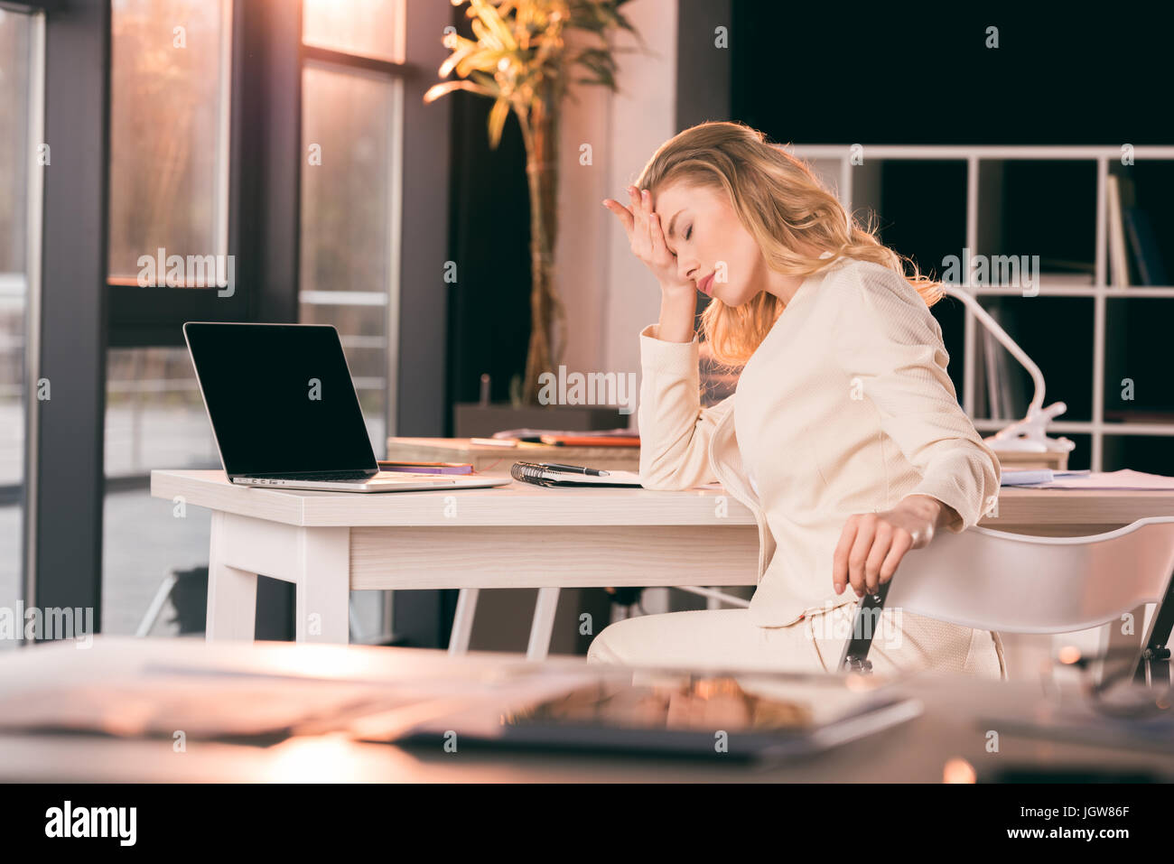 young tired businesswoman in suit sitting at table in office Stock ...