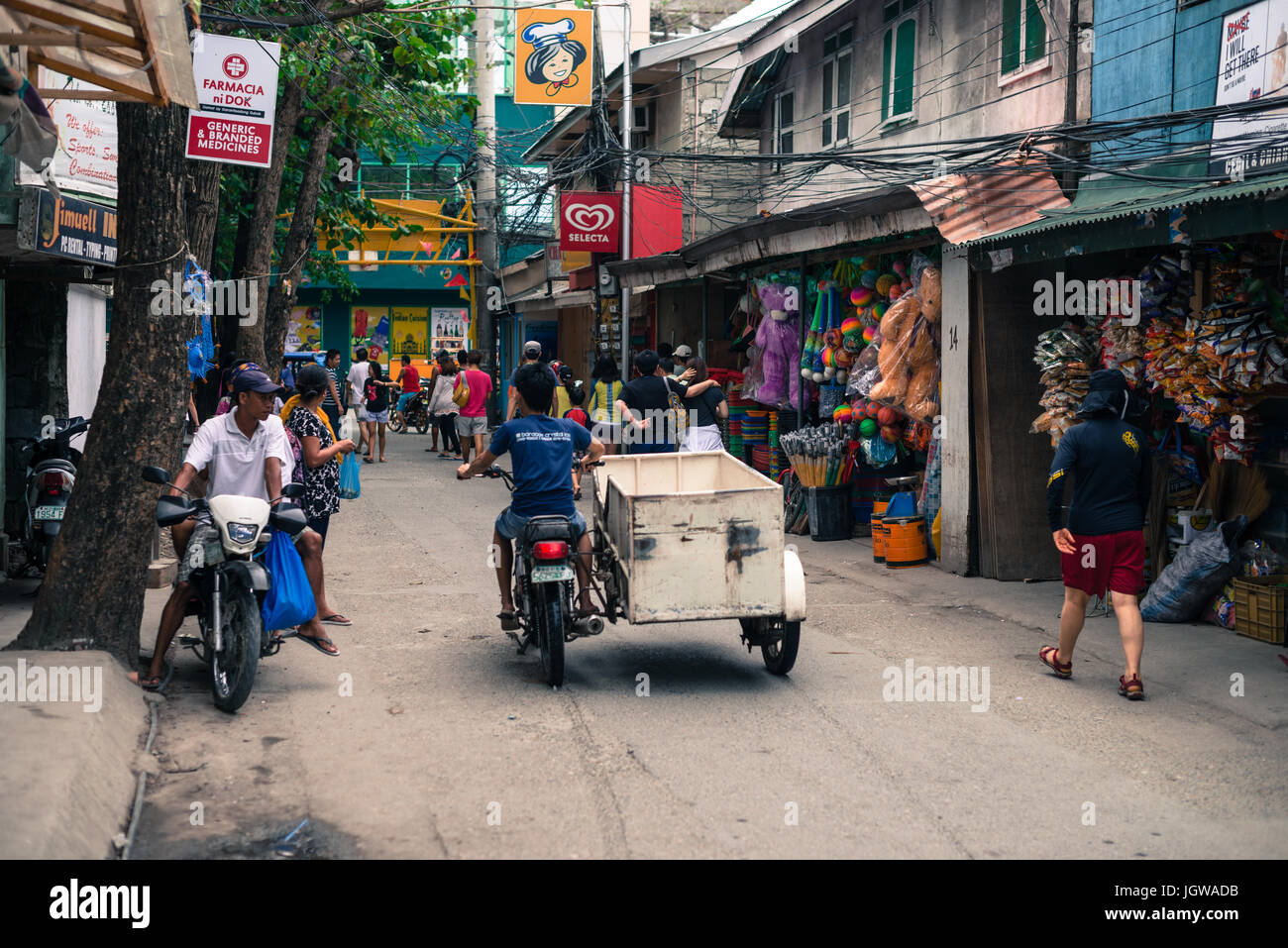 People walking and riding motorcycle in a street with many small stores ...
