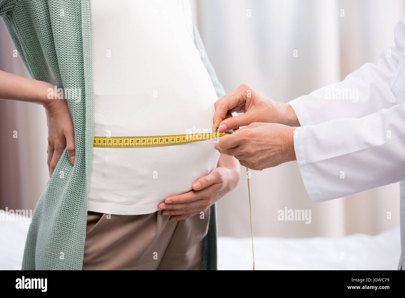 partial view of doctor measuring belly of pregnant woman in hospital ...