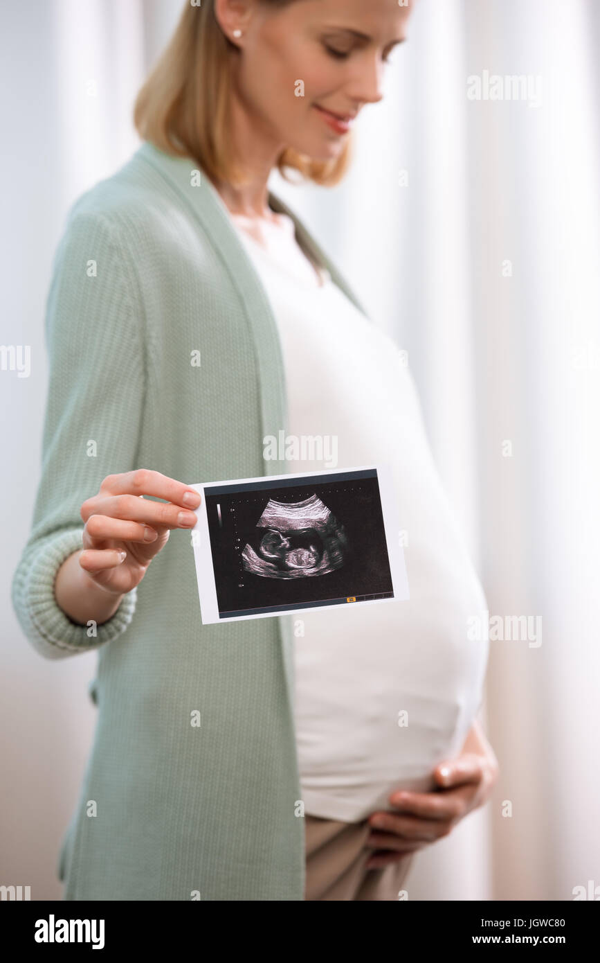 Pregnant woman holding ultrasound scan of baby and touching belly Stock ...