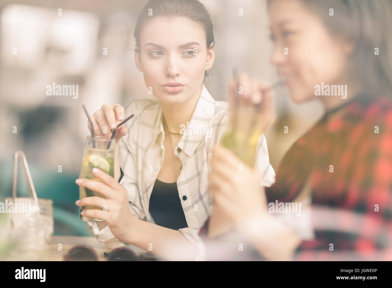 young girls drinking cocktails together while sitting at table in cafe ...