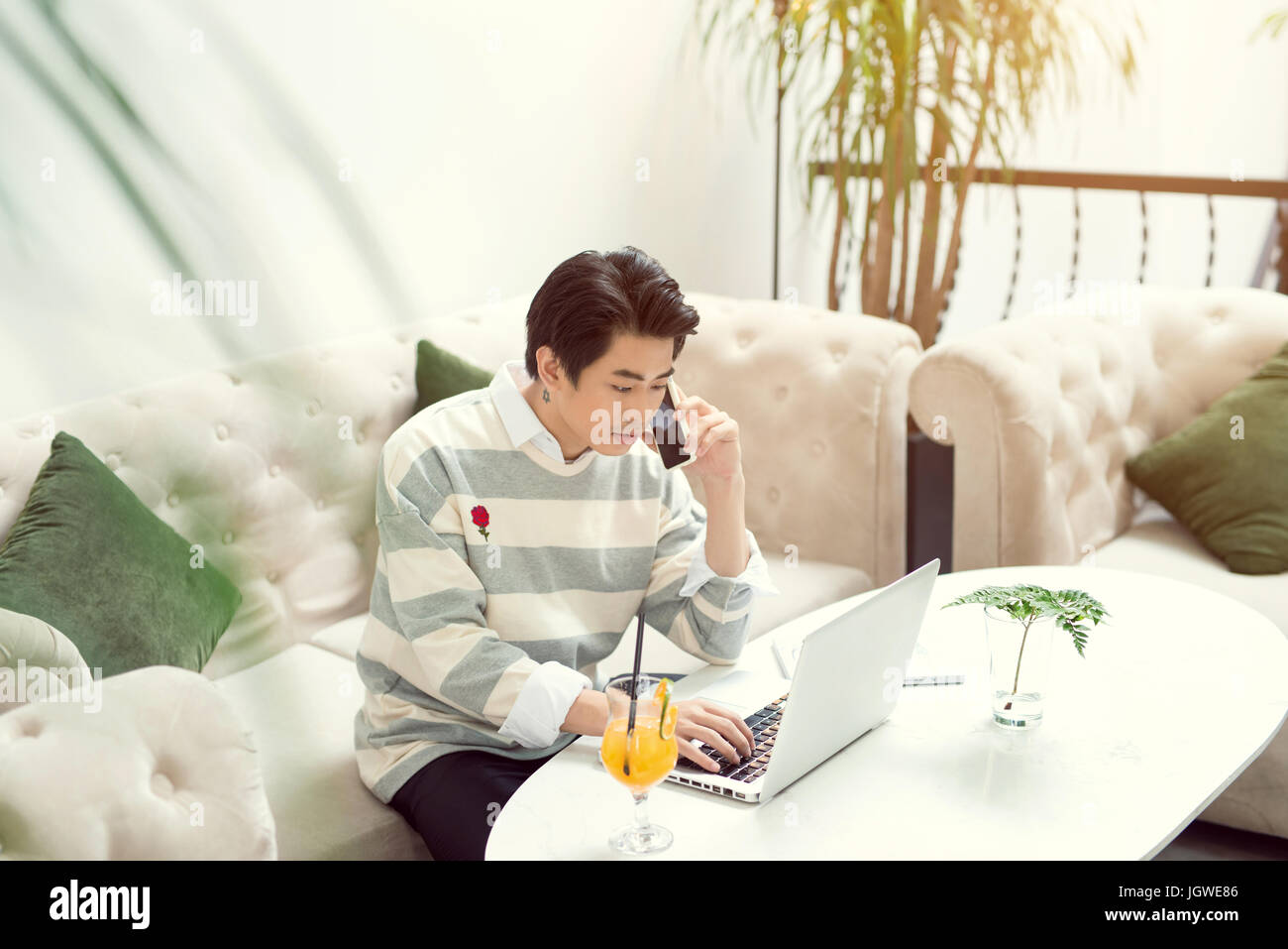 Asian businessman using mobile phone while working with laptop on table ...