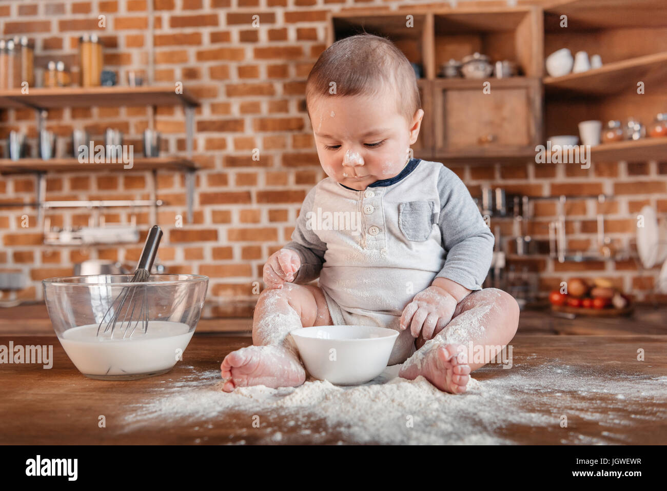 Adorable little boy playing with flour and sitting on kitchen table ...
