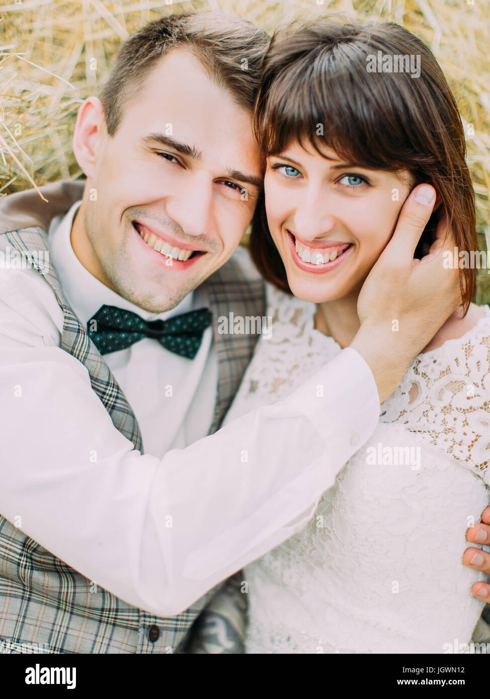The hugging smiling newlyweds are lying on the hay. The close-up ...