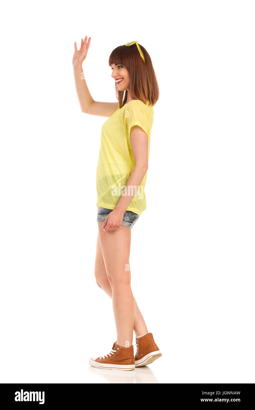 Smiling Young Woman In Yellow Shirt Jeans Shorts And Brown Sneakers