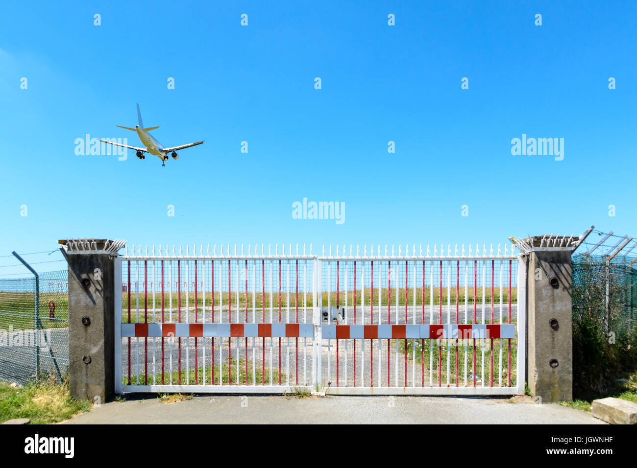 An airliner in landing approach flying above a closed fence gate with ...