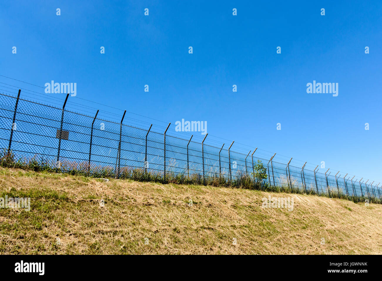 A border made of a double wire fence with barbed wire on top of a bank ...
