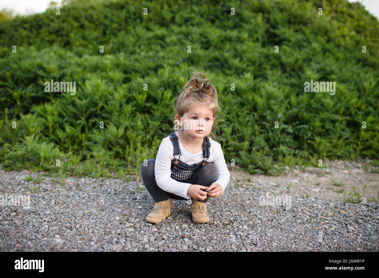 Cute girl crouching on dirt track looking away Stock Photo - Alamy