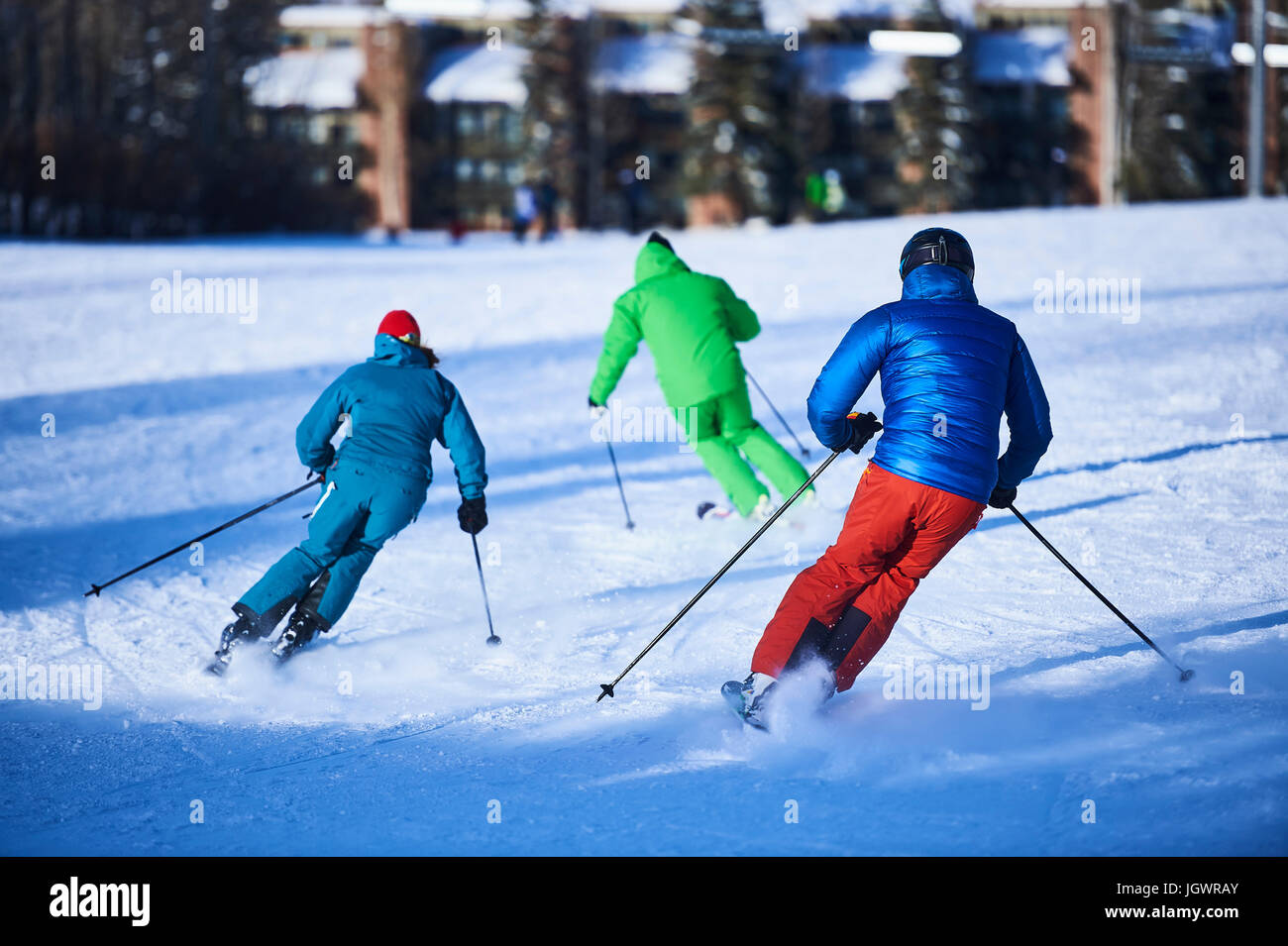 Rear view of male and female skiers skiing down snow covered ski slope ...