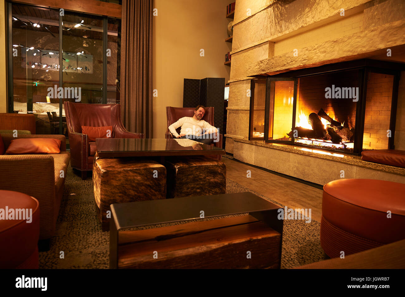 Portrait of man relaxing in armchair by log fire in hotel lounge, Aspen ...